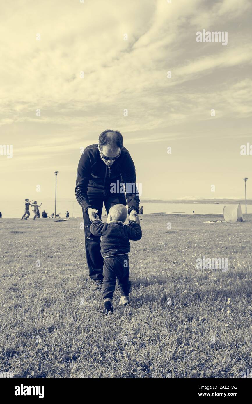 Cute baby girl learning to walk with her father in a park Stock Photo ...