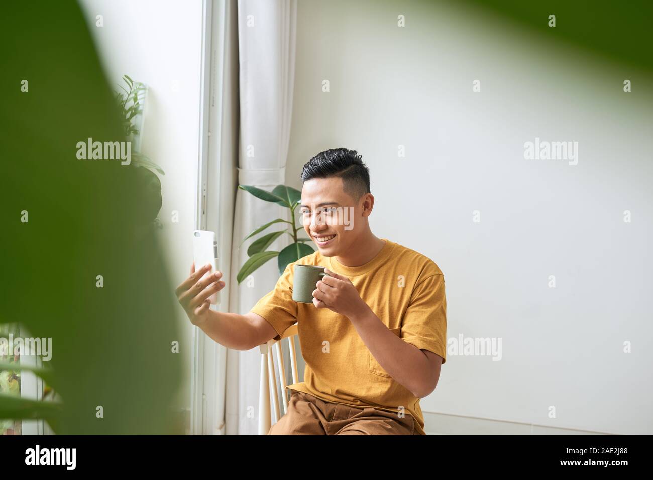 Portrait of handsome young man with smartphone near window Stock Photo ...