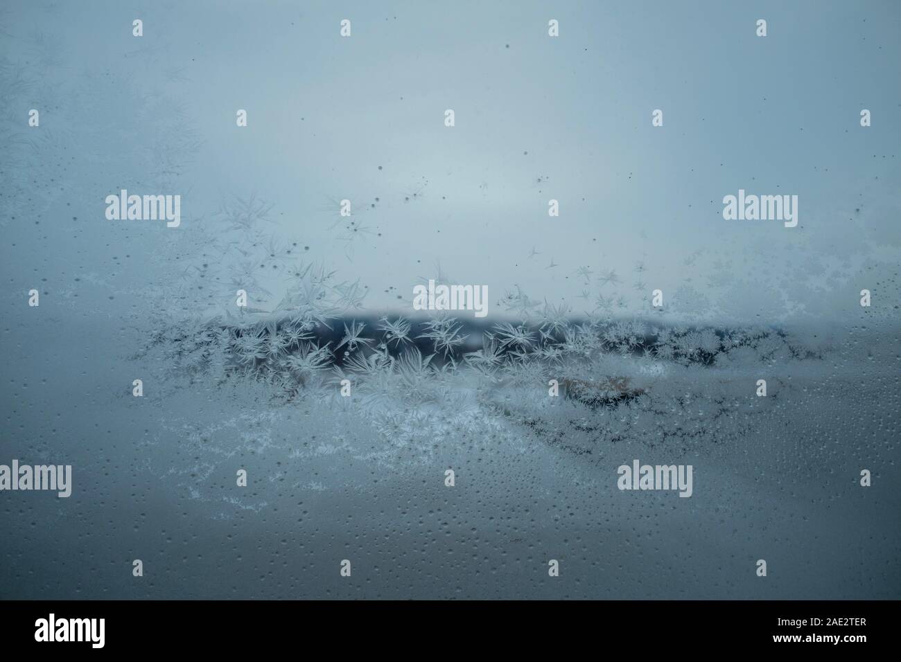 Frozen window glass with frosty pattern and dark grey winter landscape ...