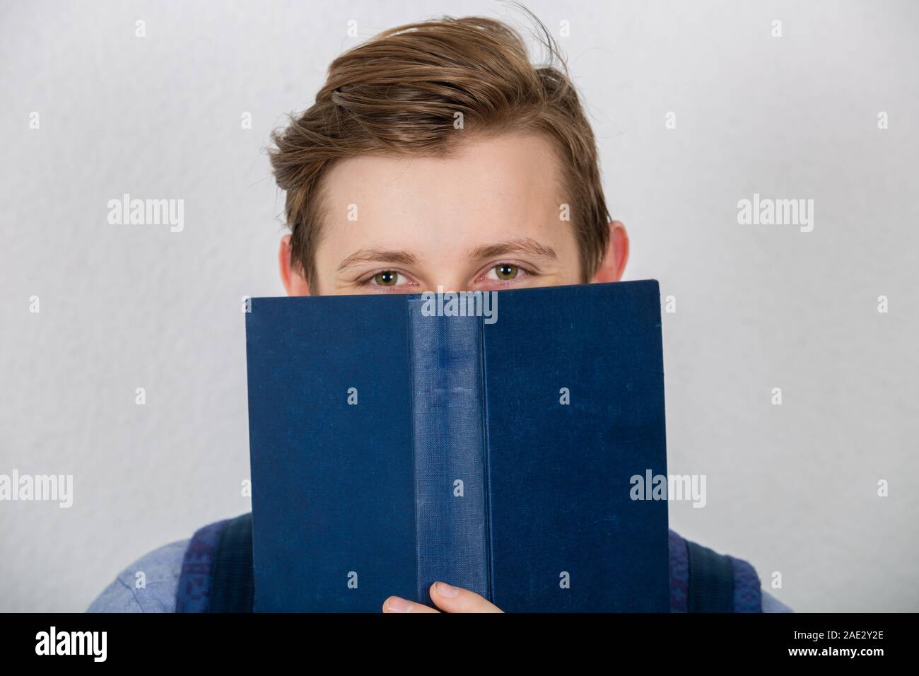 Happy teenager boy smiling covering half face with a opened blue book ...