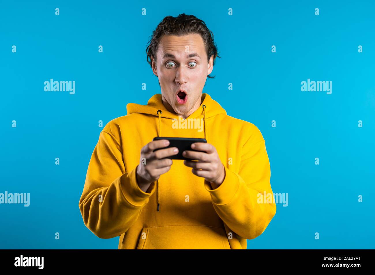 Handsome man playing game on smartphone on blue studio wall. Using ...