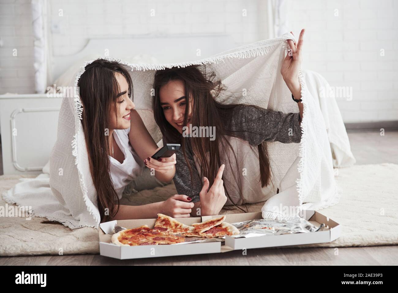 Hiding under warm blanket. Sisters eating pizza when watching TV while ...