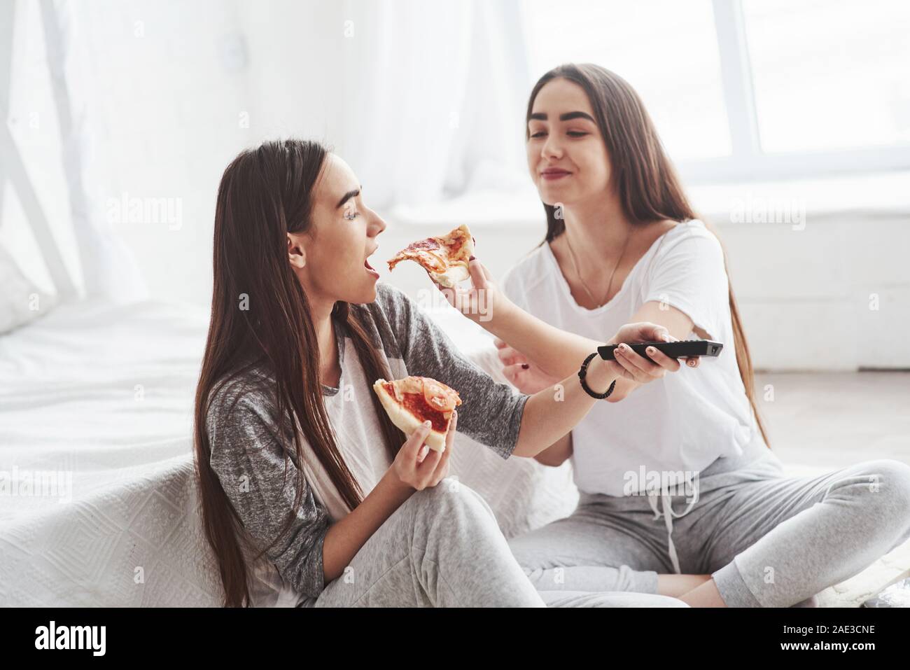 Taste mine slice. Sisters eating pizza when watching TV while sits on ...