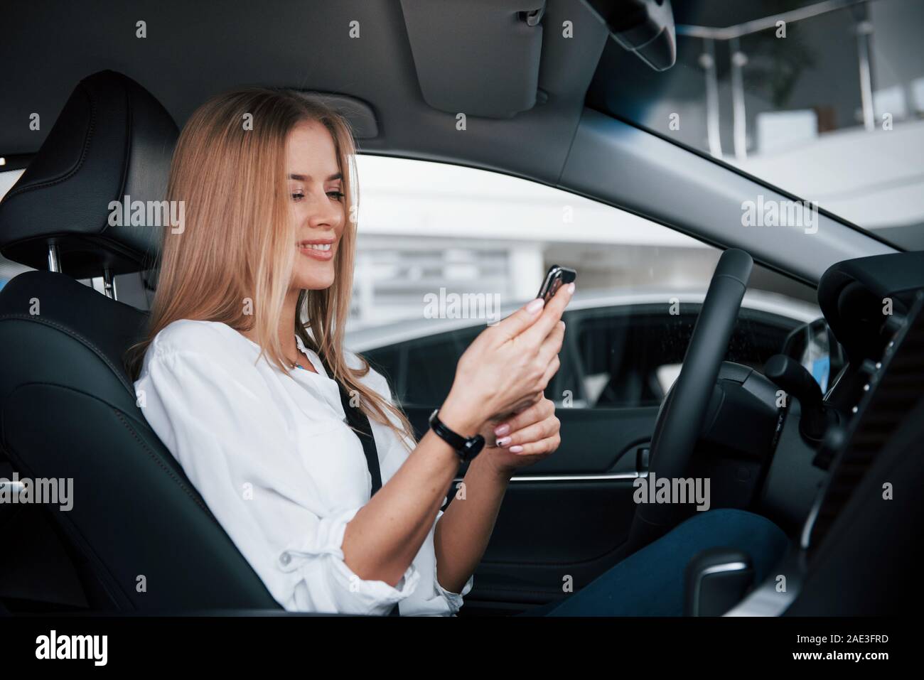 Texting in the smartphone. Beautiful blonde girl sitting in the new car ...