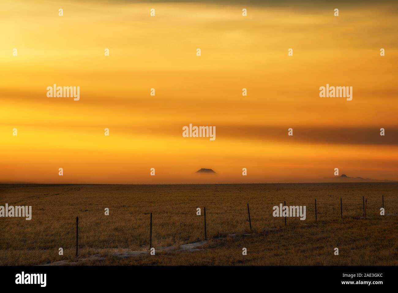 A fooggy morning sunrise over fenced pasture land with a mountain peak ...