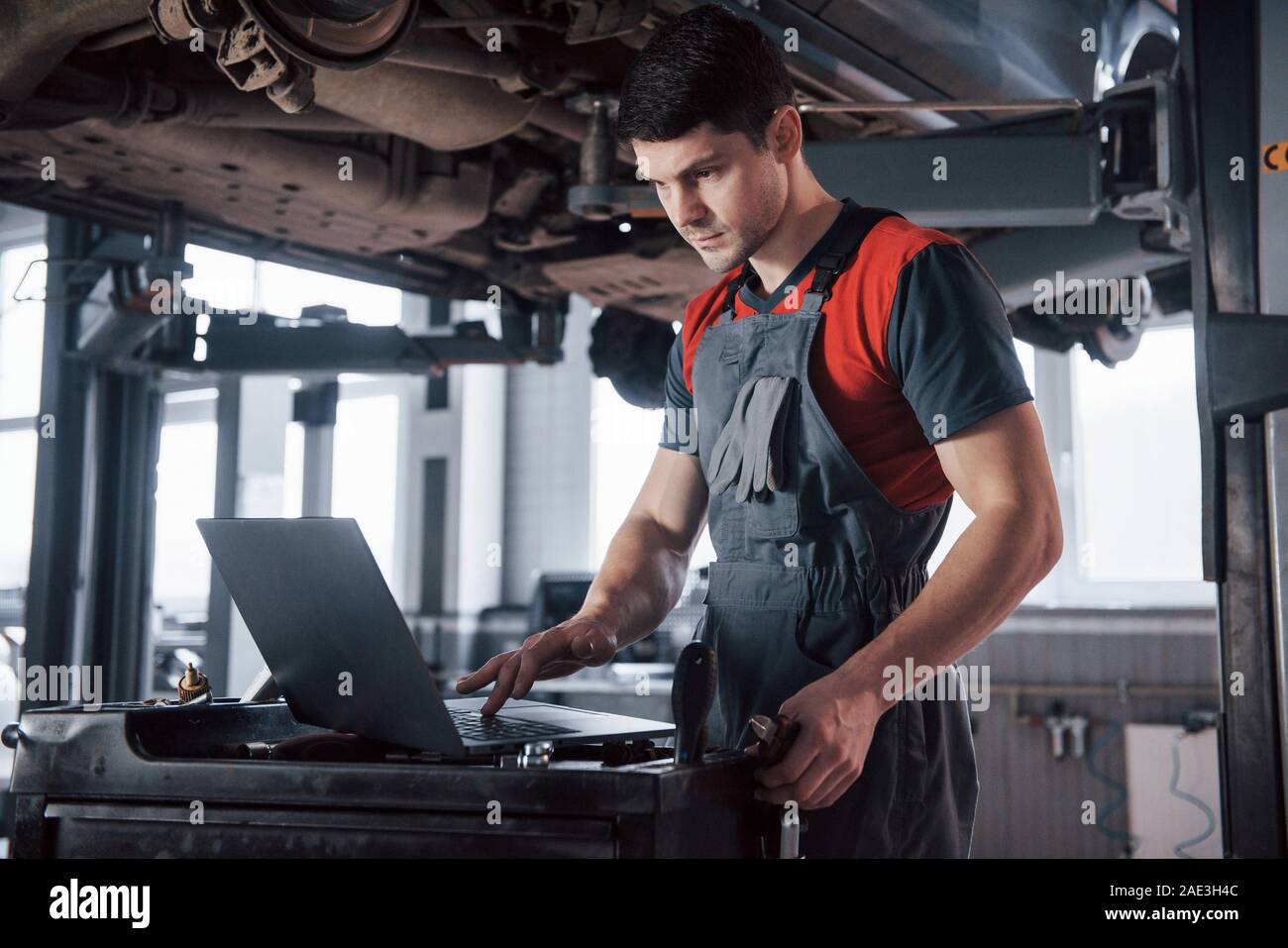Silver colored device. Man at the workshop in uniform using laptop for ...