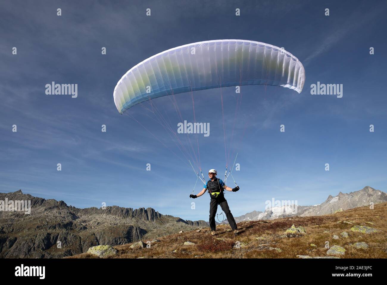 Paraglider Pilot stands on a slope and balances his paraglider above ...