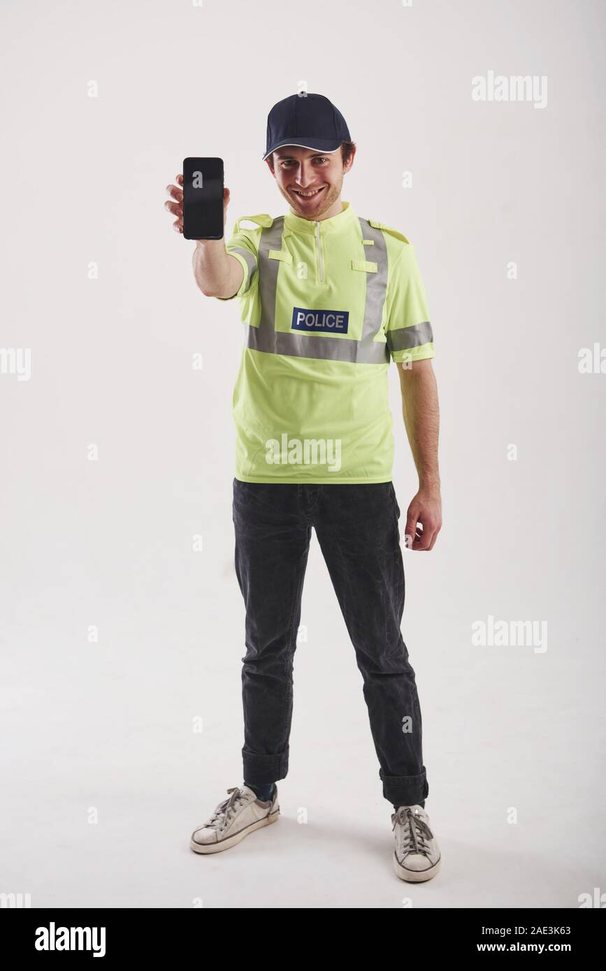 Smartphone in the hand. Policeman in green uniform stands against white ...