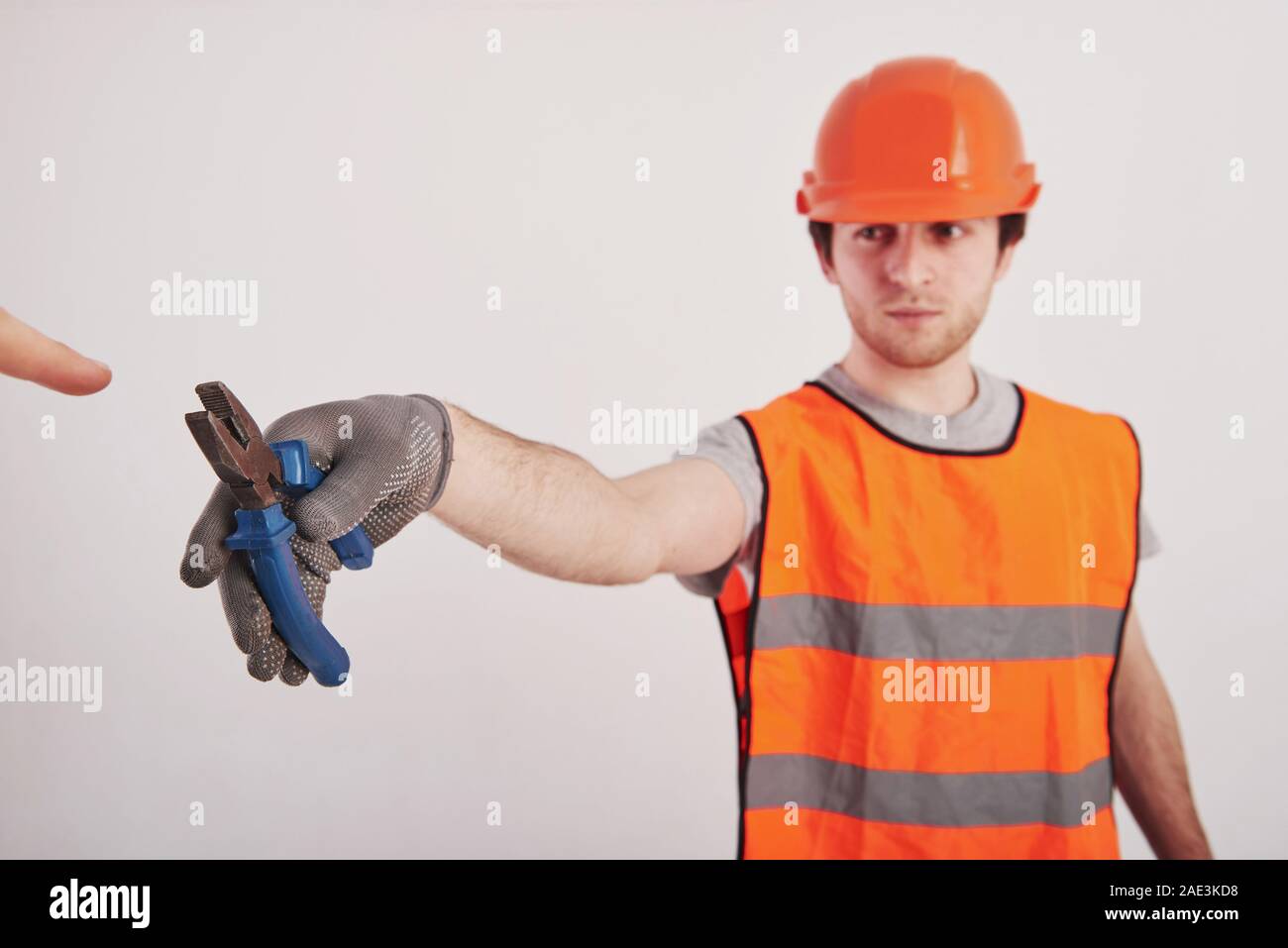 Another person takes the tool. Man in orange colored uniform stands ...