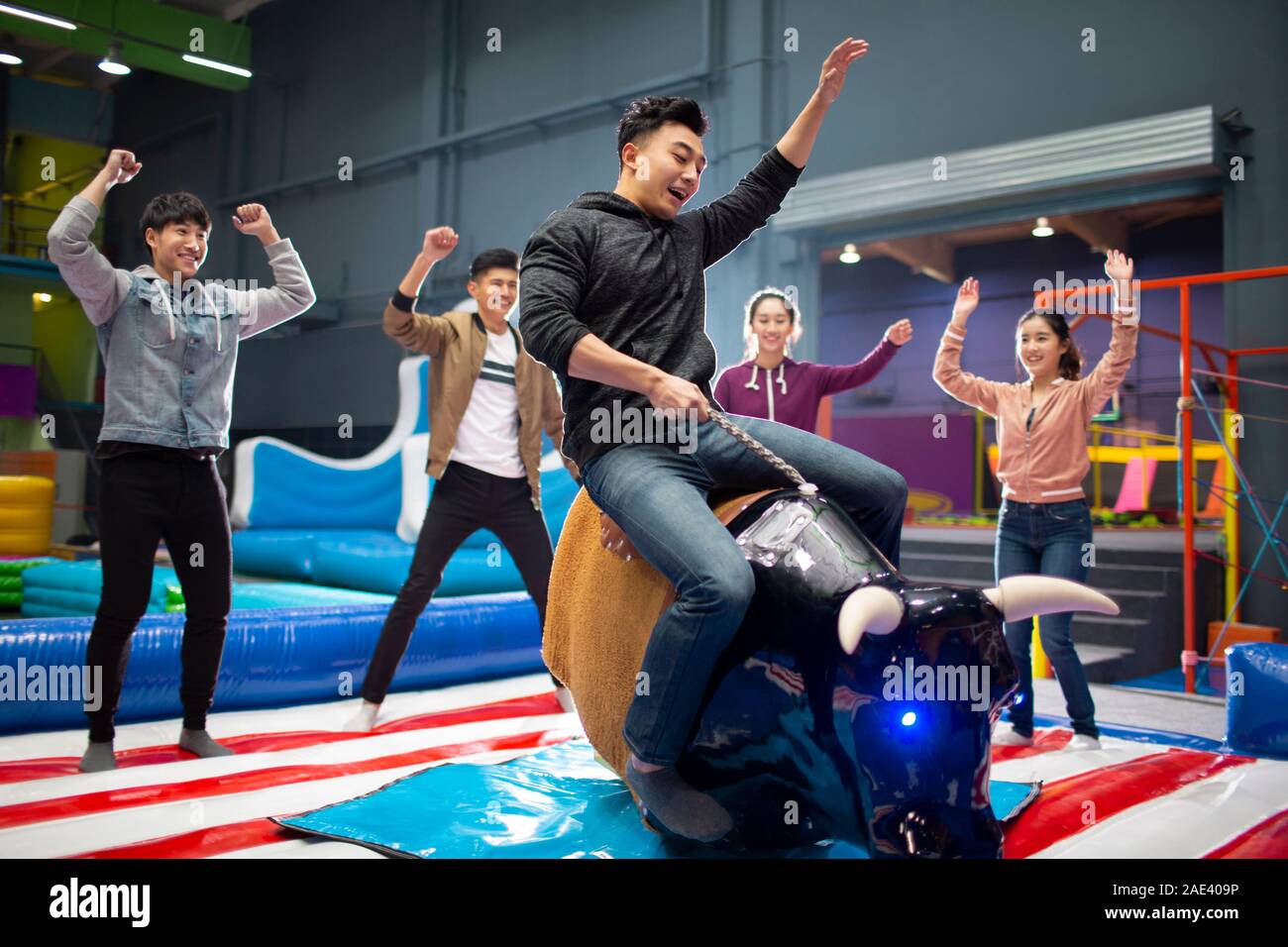 Happy young friends playing mechanical bull game Stock Photo - Alamy