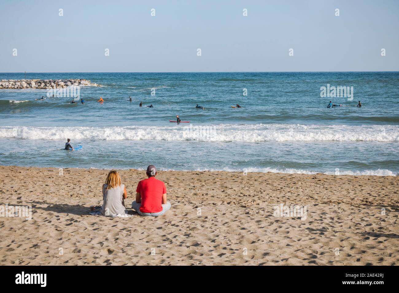 A couple on beach watching surfers, surfing on high waves, rough sea ...