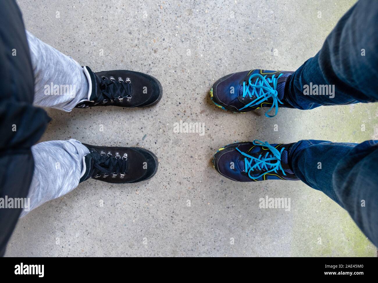 Two pair of legs in boots for hiking stand on the grey pavement. Top ...