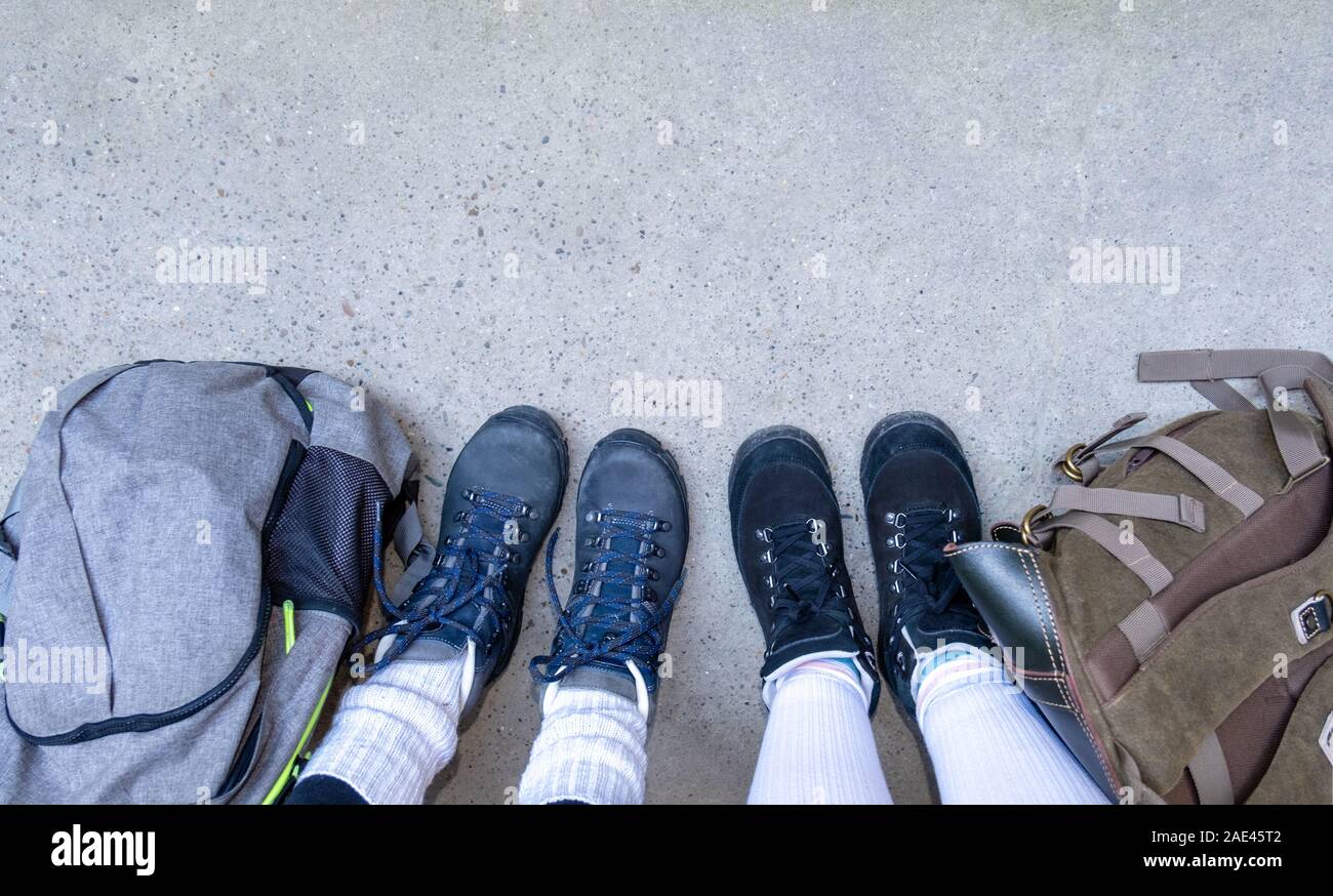 Two pair of legs in boots for hiking stand on the grey pavement with ...