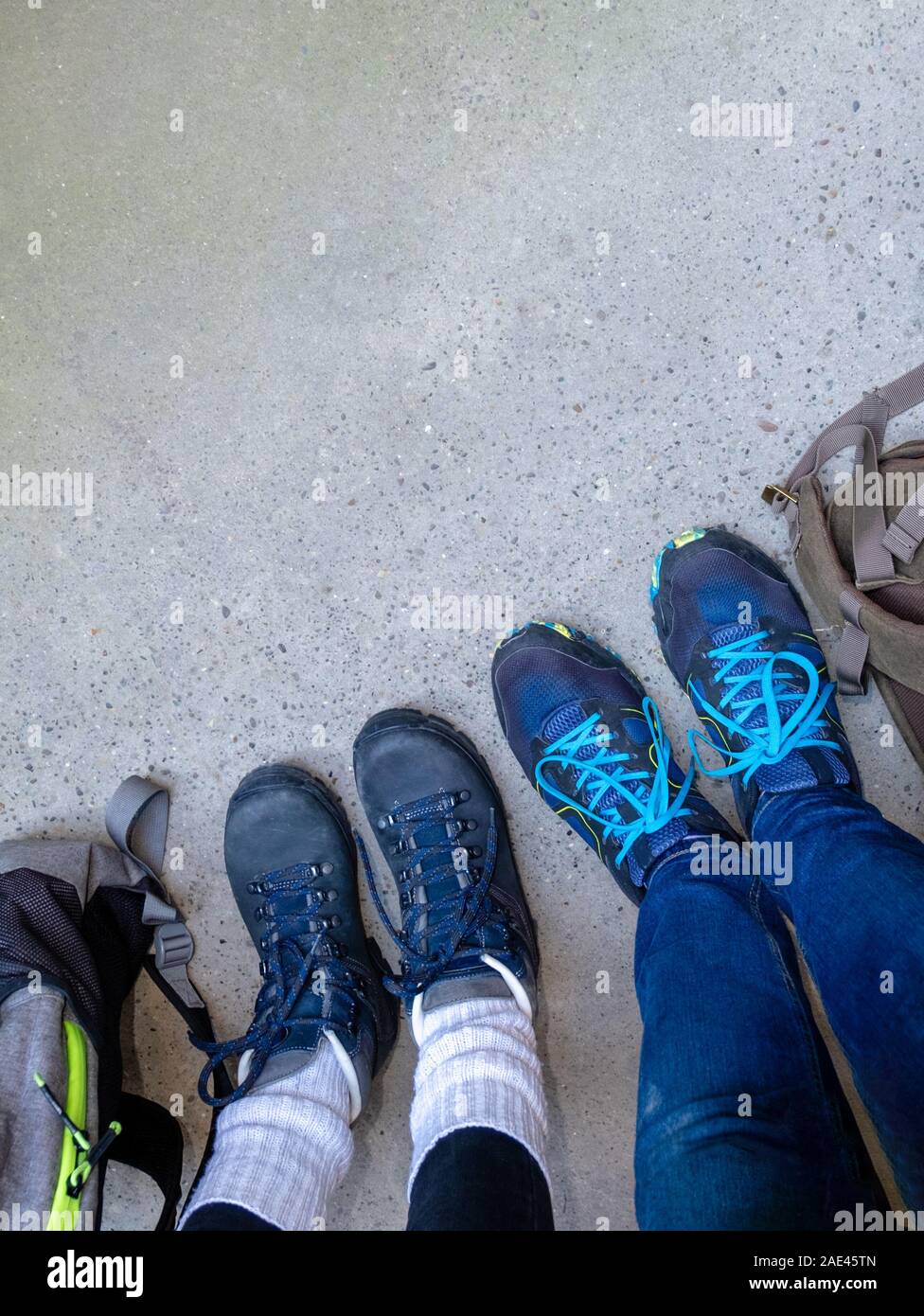 Two pair of legs in boots for hiking stand on the grey pavement with ...