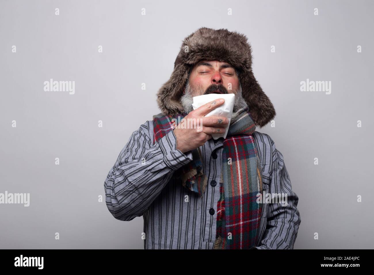 The man is sick and sneezing with hat and scarf on a gray background ...