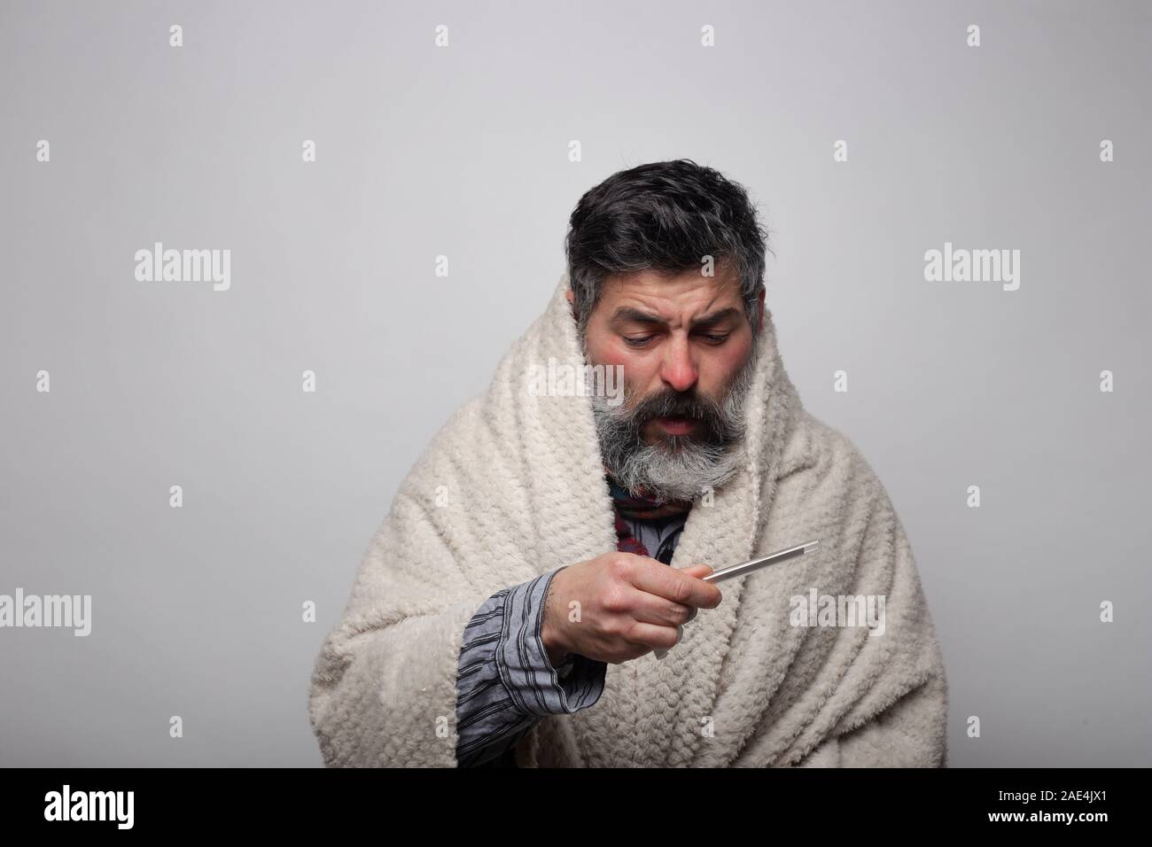 Sick mature man looking at the thermometer wrapped in a blanket. health ...