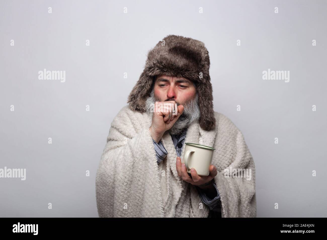 Man with flu and cough sheltered with hat and blanket on gray ...