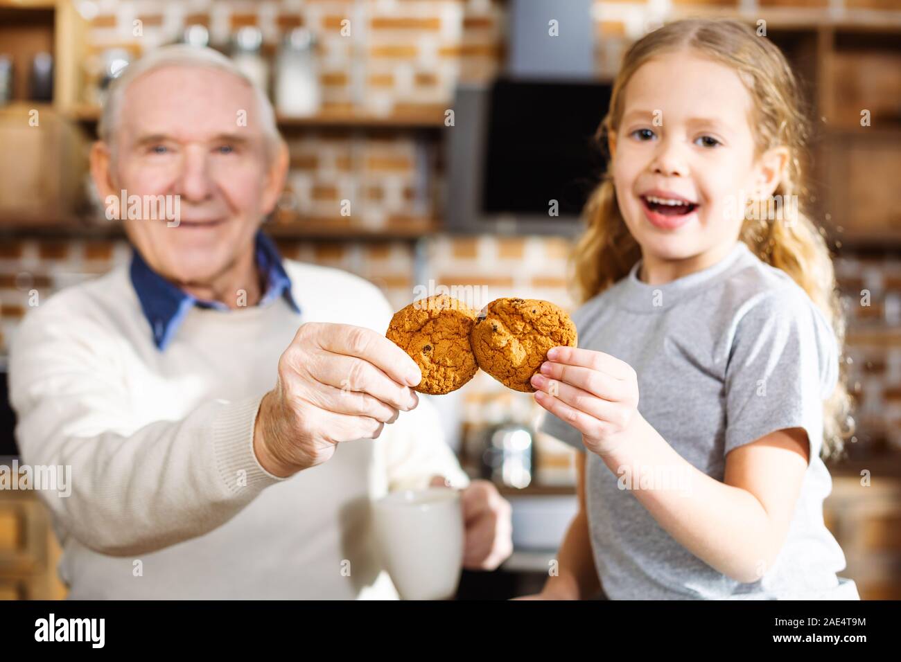 Cheerful elderly man eating cookies with his granddaughter Stock Photo ...