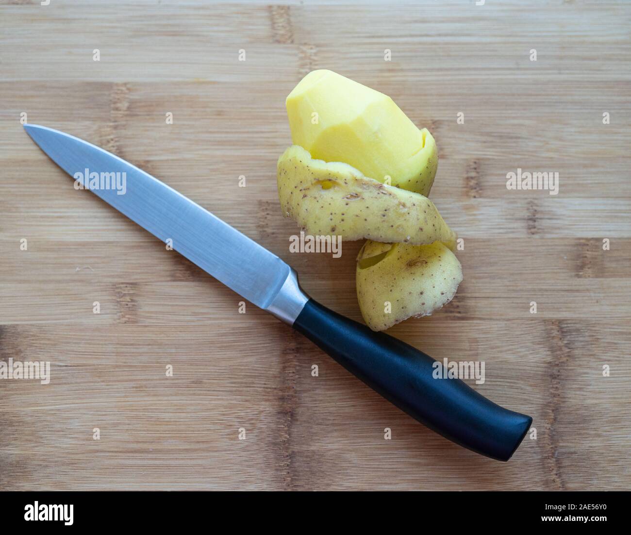 Peeled potatoes and a sharp knife on the background of a wooden surface ...