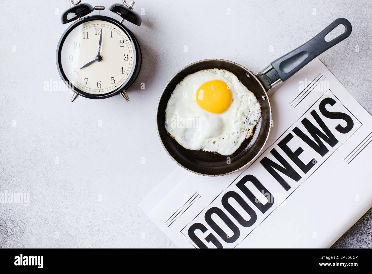 Breakfast time. Fried eggs in a pan with an alarm clock and a newspaper ...