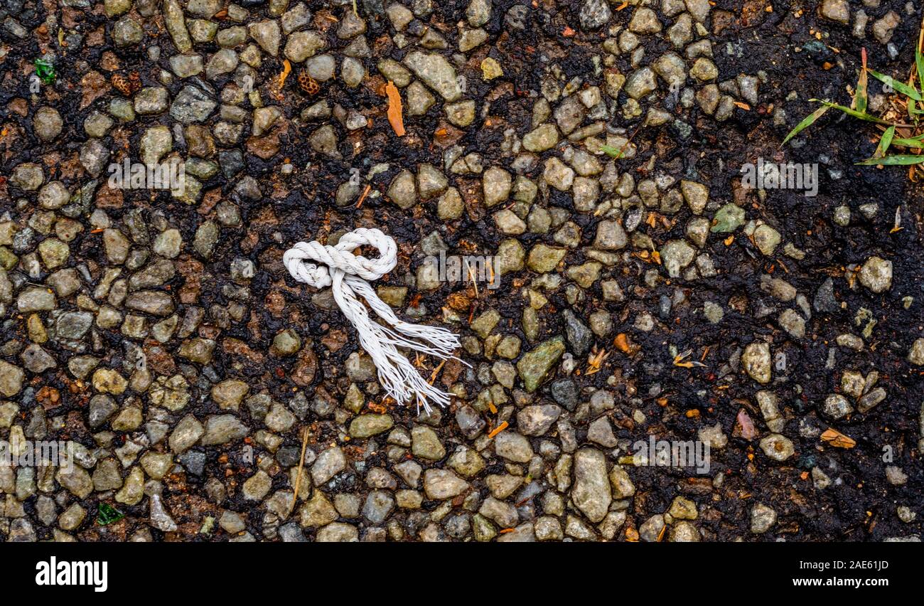 A piece of braided plastic rope isolated on a bitumen surface outdoors ...