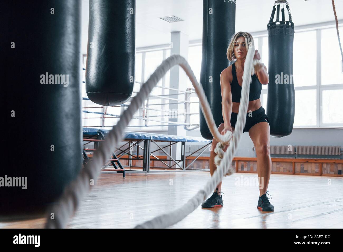 Front view. Blonde sport woman have exercise with ropes in the gym ...