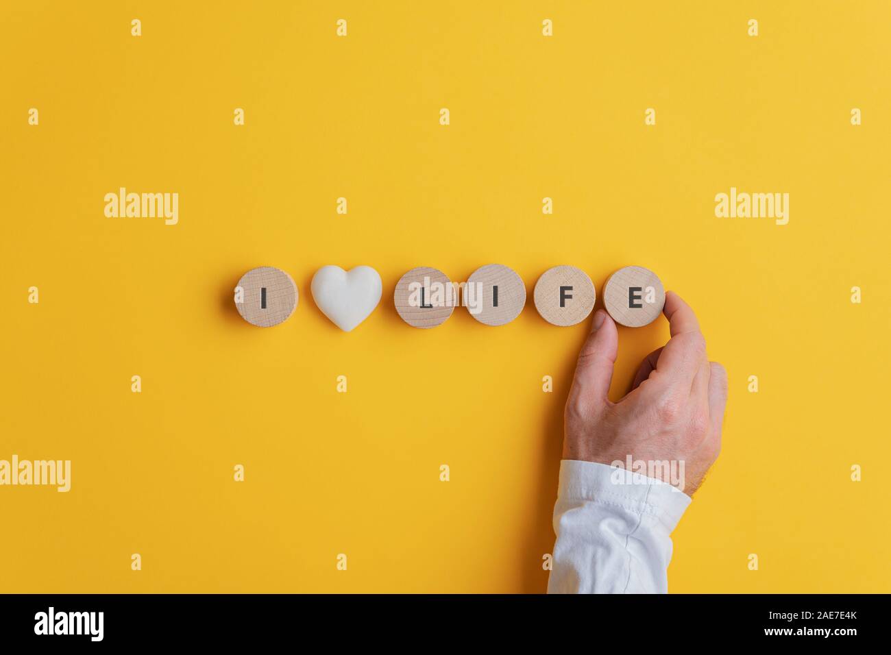 Male hand making an I love life sign spelled on wooden cut circles with ...