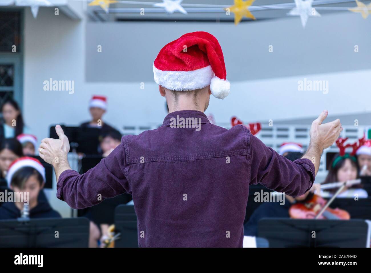 Back view of a male conductor, wearing casual outfit with red santa hat ...