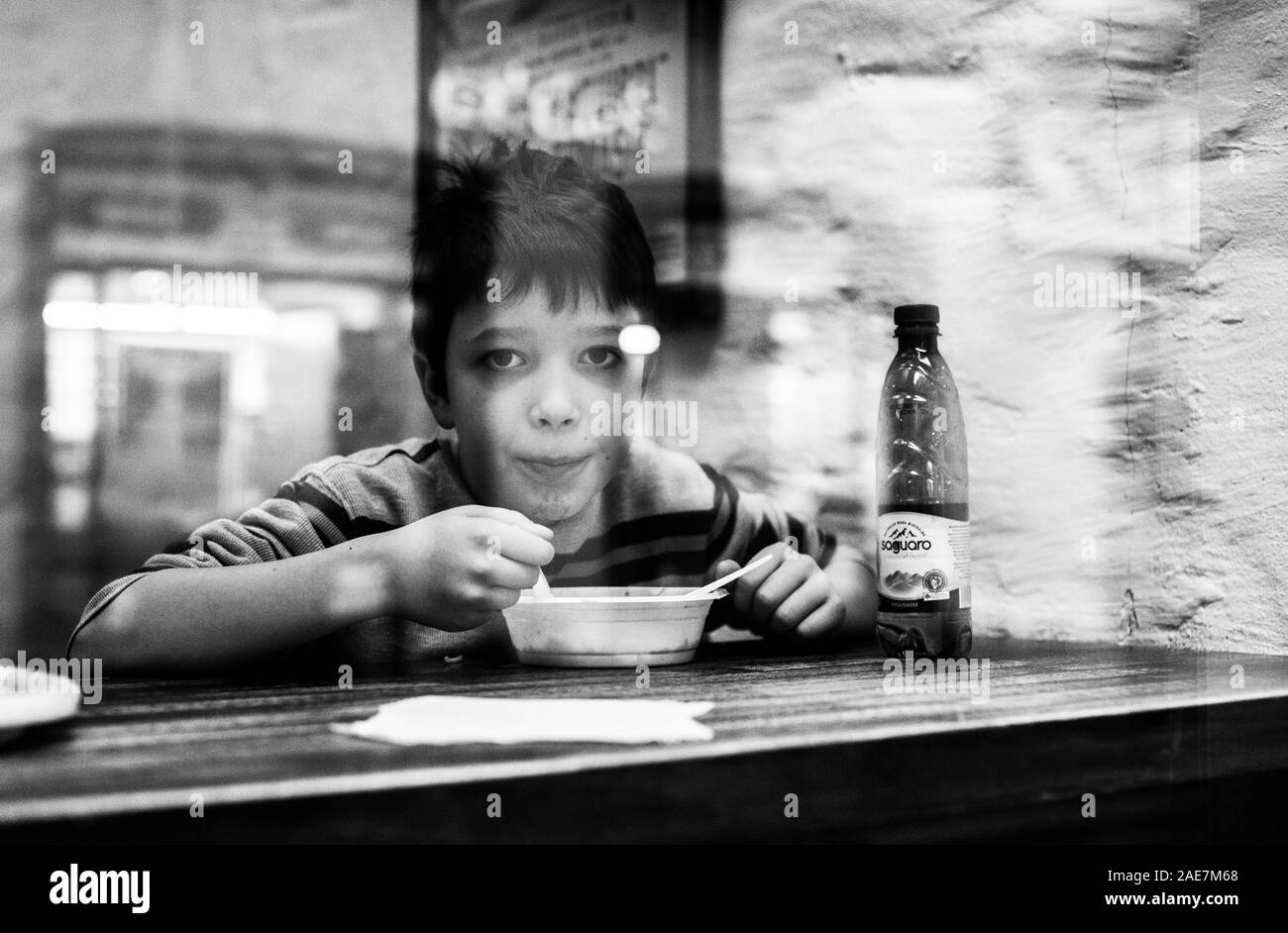 A boy eating pasta from outside a restaurant window, shadows and light ...