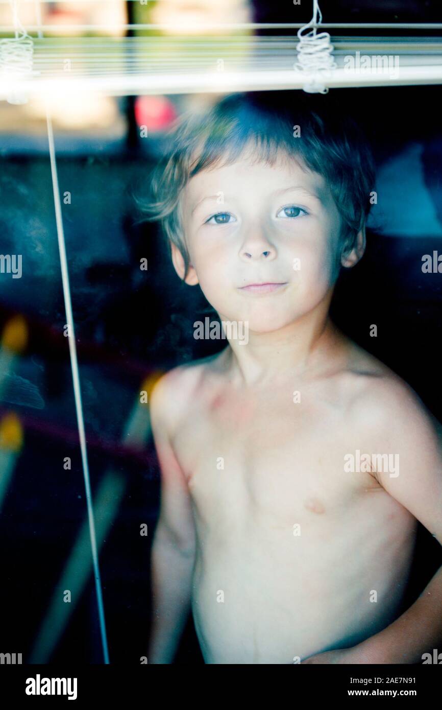 Little cute boy throught window making funny faces, home alone ...