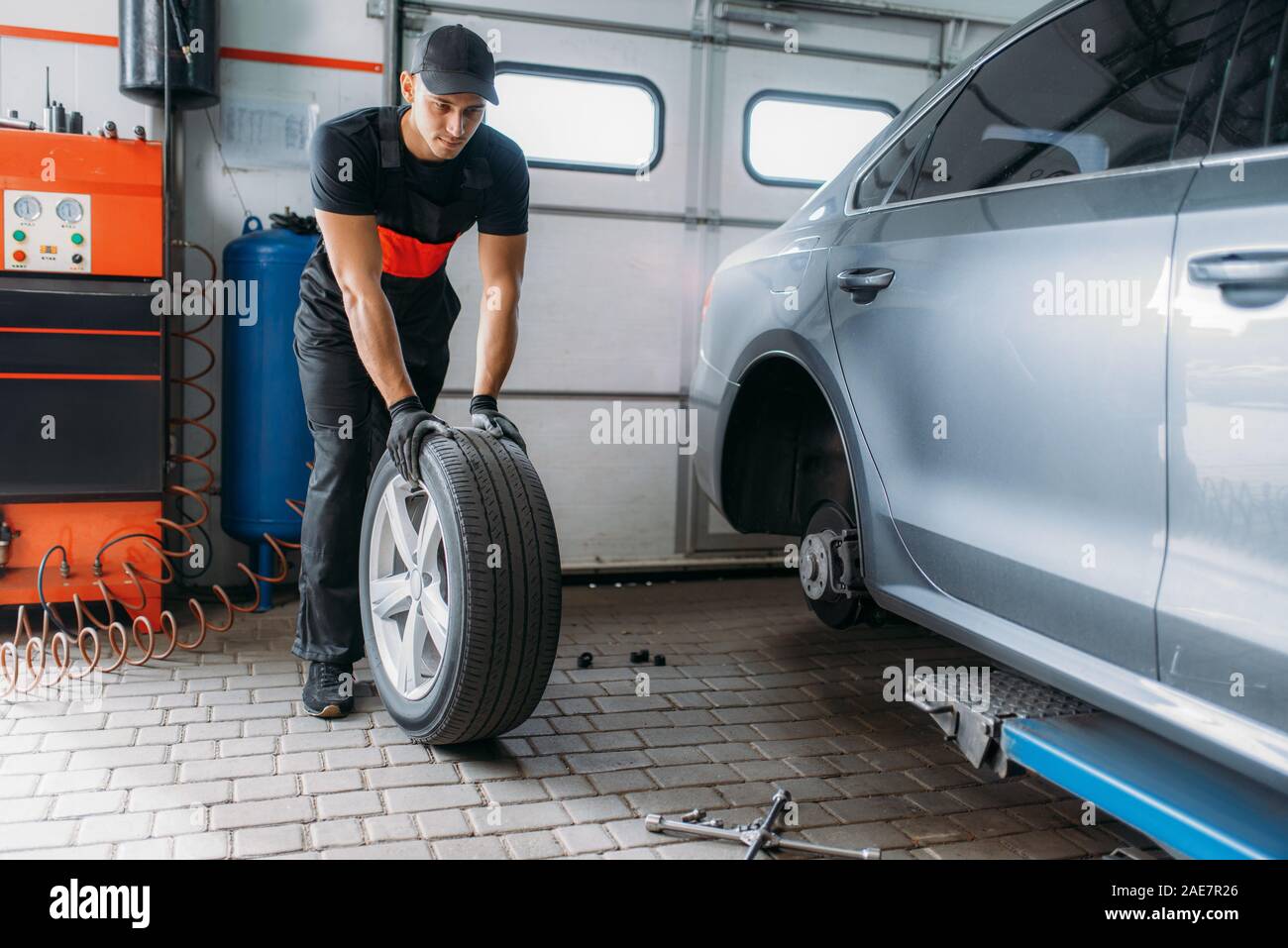 Auto mechanic in uniform holds wheel, tire service Stock Photo - Alamy