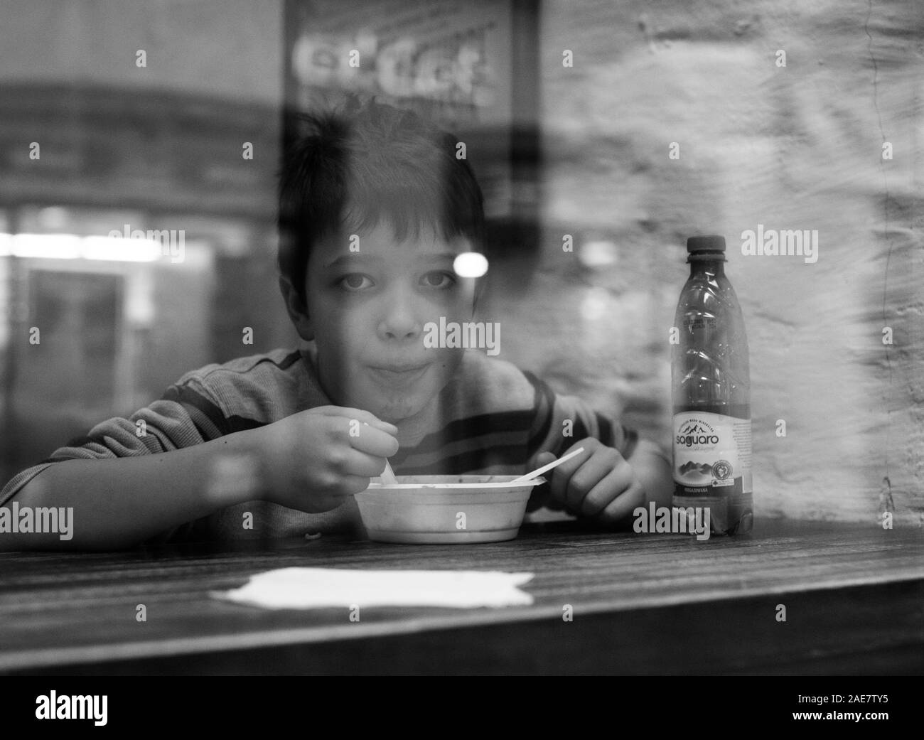 A boy eating pasta from outside a restaurant window, shadows and light ...
