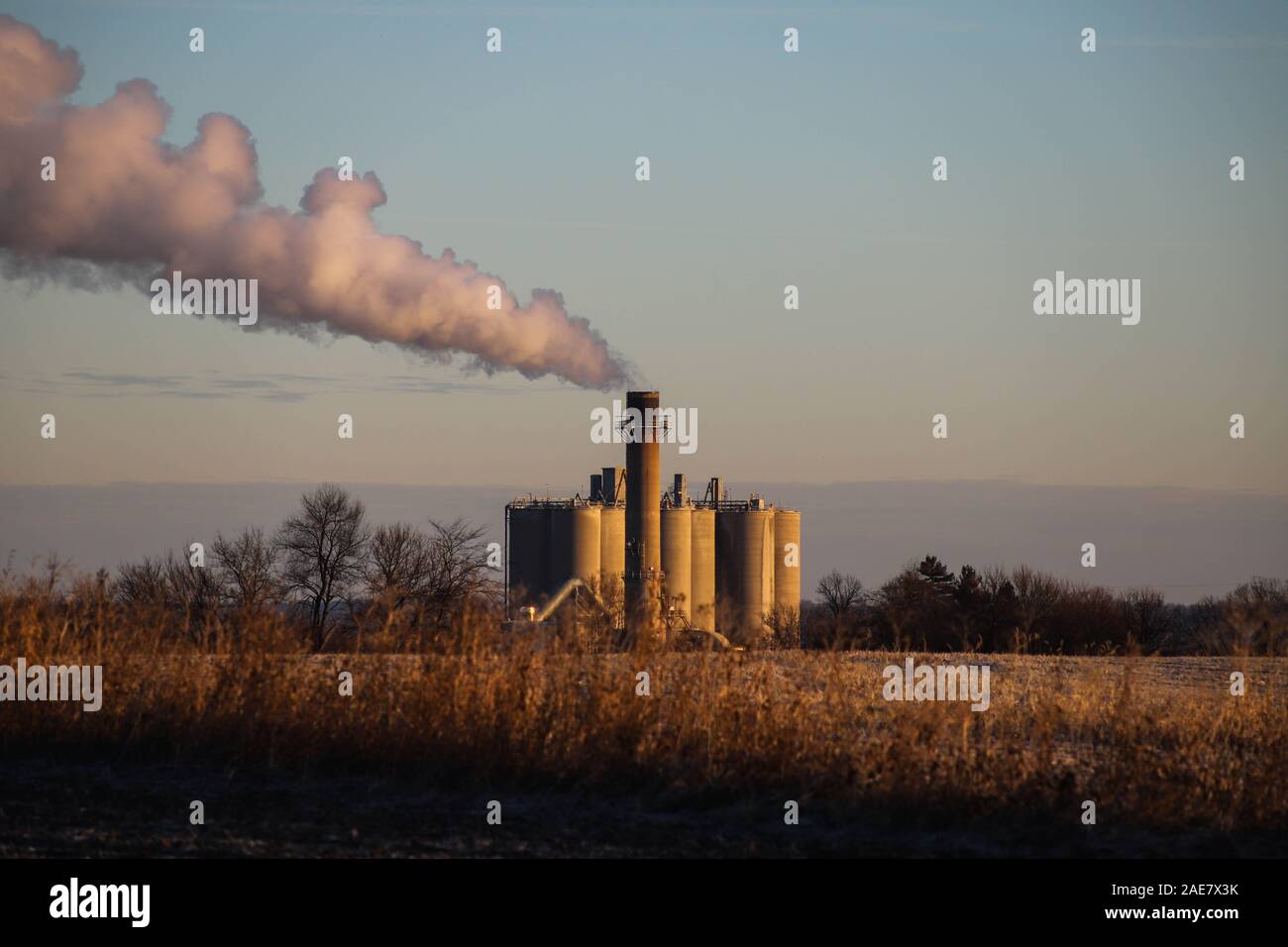 Smoke / steam leaving a smoke stack from a factory with concrete silos ...