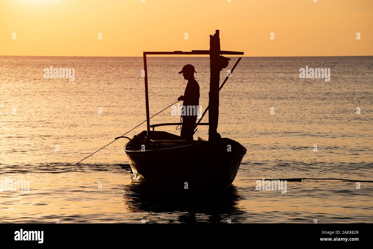 Silhouette of boat and fisherman with warm and sunset low lighting dark ...
