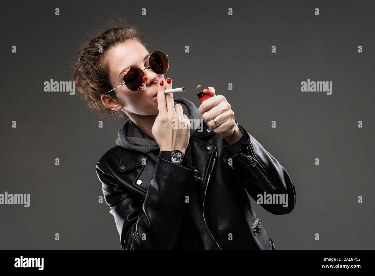 Caucasian girl with rough facial features in a black jacket lights a ...