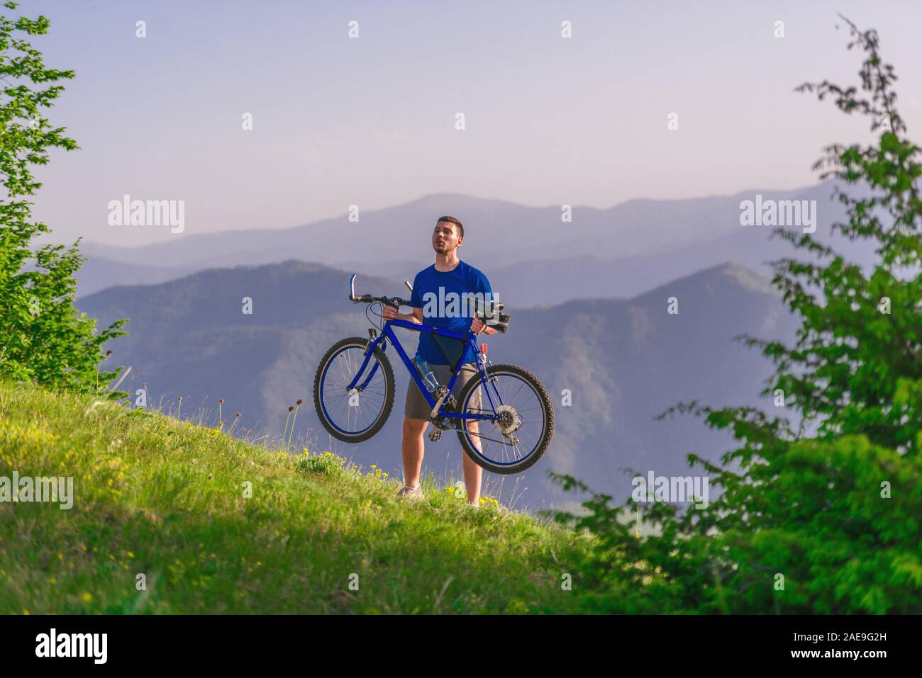 Tired cyclist is wiping his sweat off his face while pushing his ...
