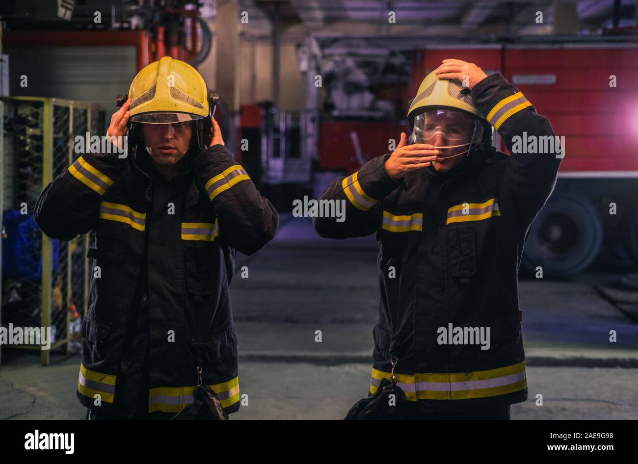 Portrait of two young firemen in uniform standing inside the fire ...