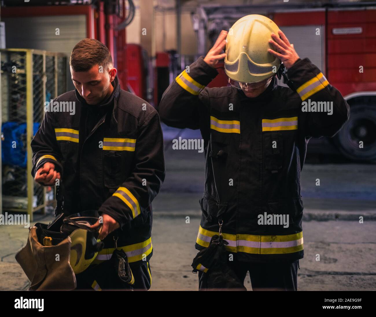 Portrait of two young firemen in uniform standing inside the fire ...