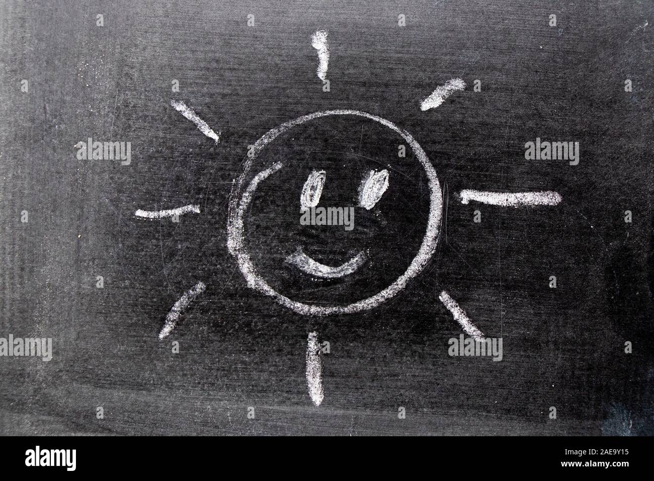 White color chalk hand drawing in sun with ray shape on blackboard ...