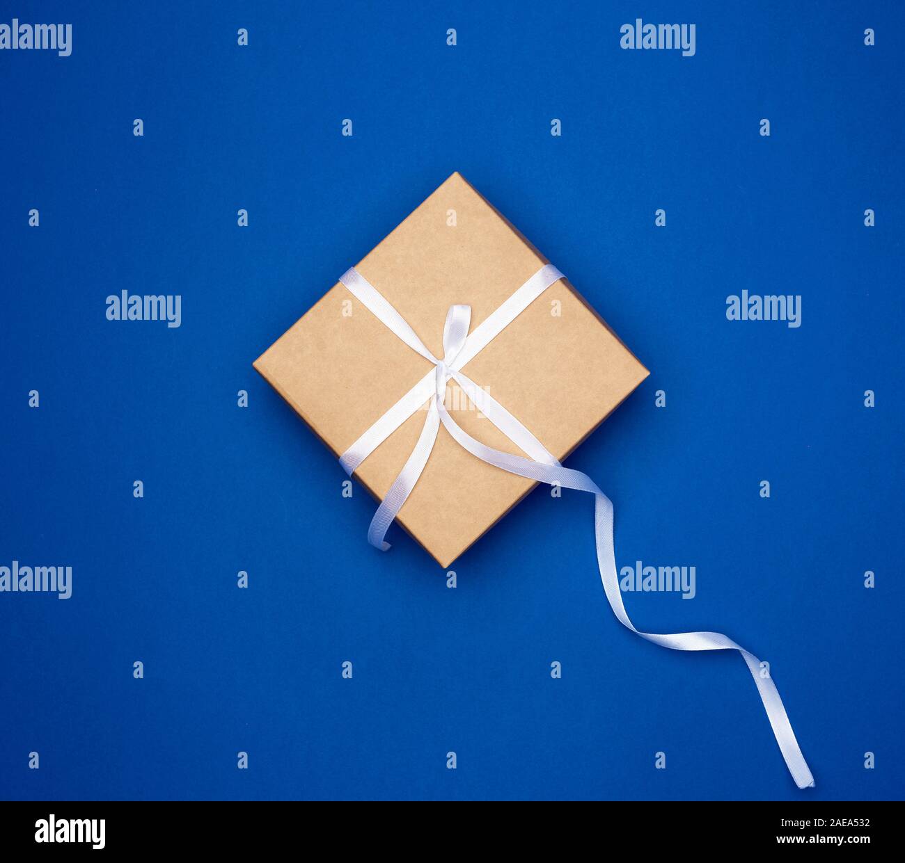 cardboard gift square box tied with a white thin ribbon on a dark blue ...