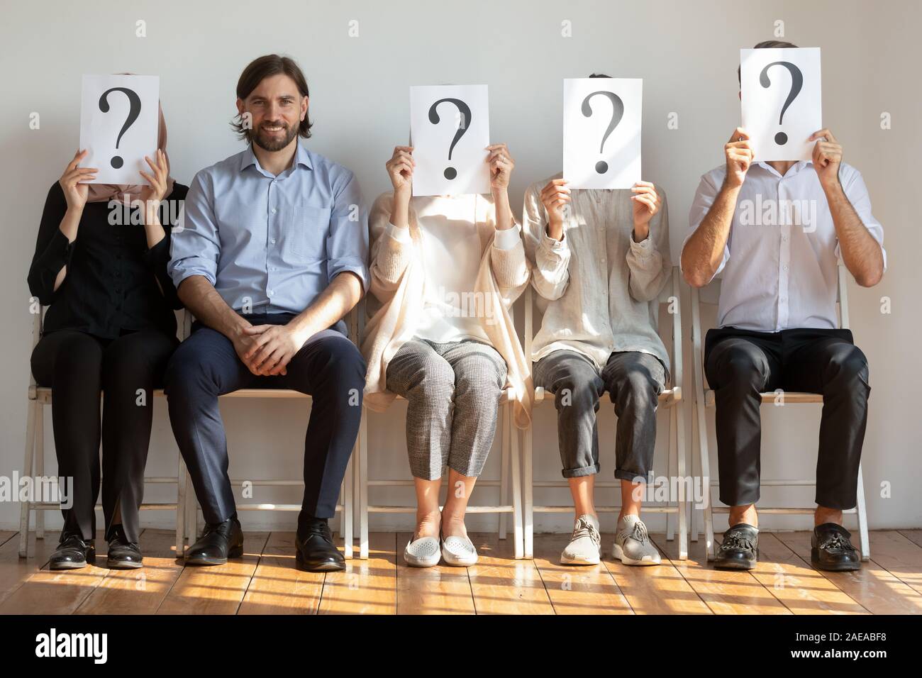 Confident young man sitting on chair in queue of unknown people Stock ...