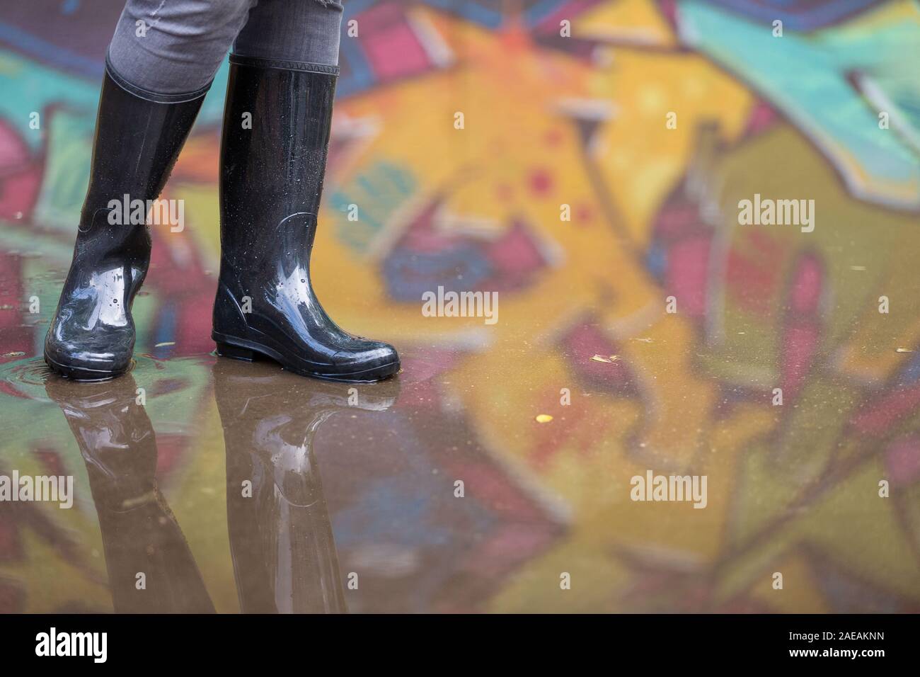 Girl in rubber boots standing in the puddle in the street. Woman in ...