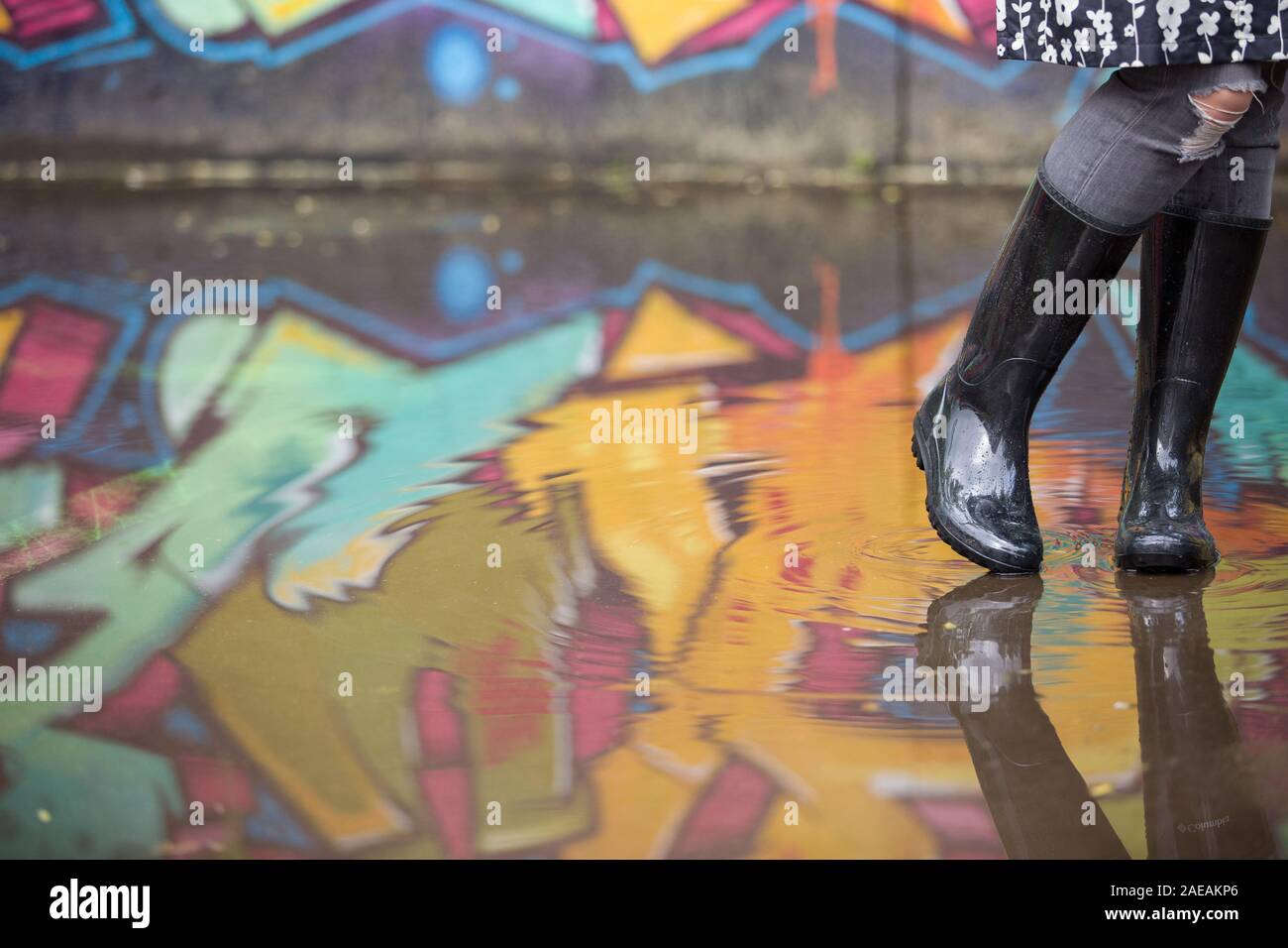 Girl in rubber boots standing in the puddle in the street. Woman in ...