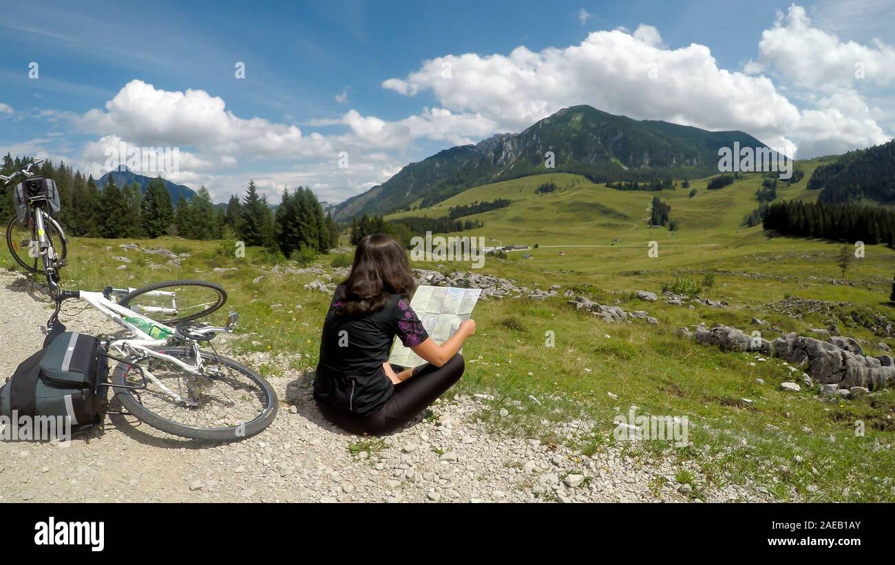 Summer time in the Austrian alps. Young woman on a cycling trip. Beautiful cyclist planning a ...