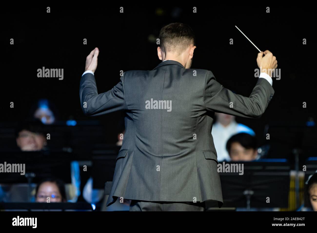 Back view of a male band conductor in formal suit conducting his ...