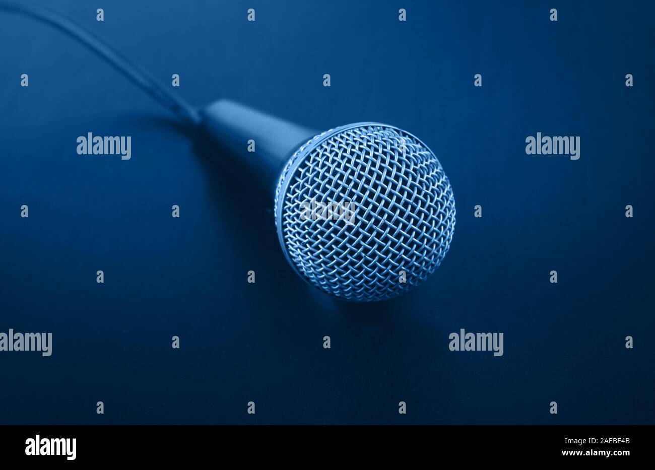 Close up classic wired vocal microphone with cable over dark blue ...