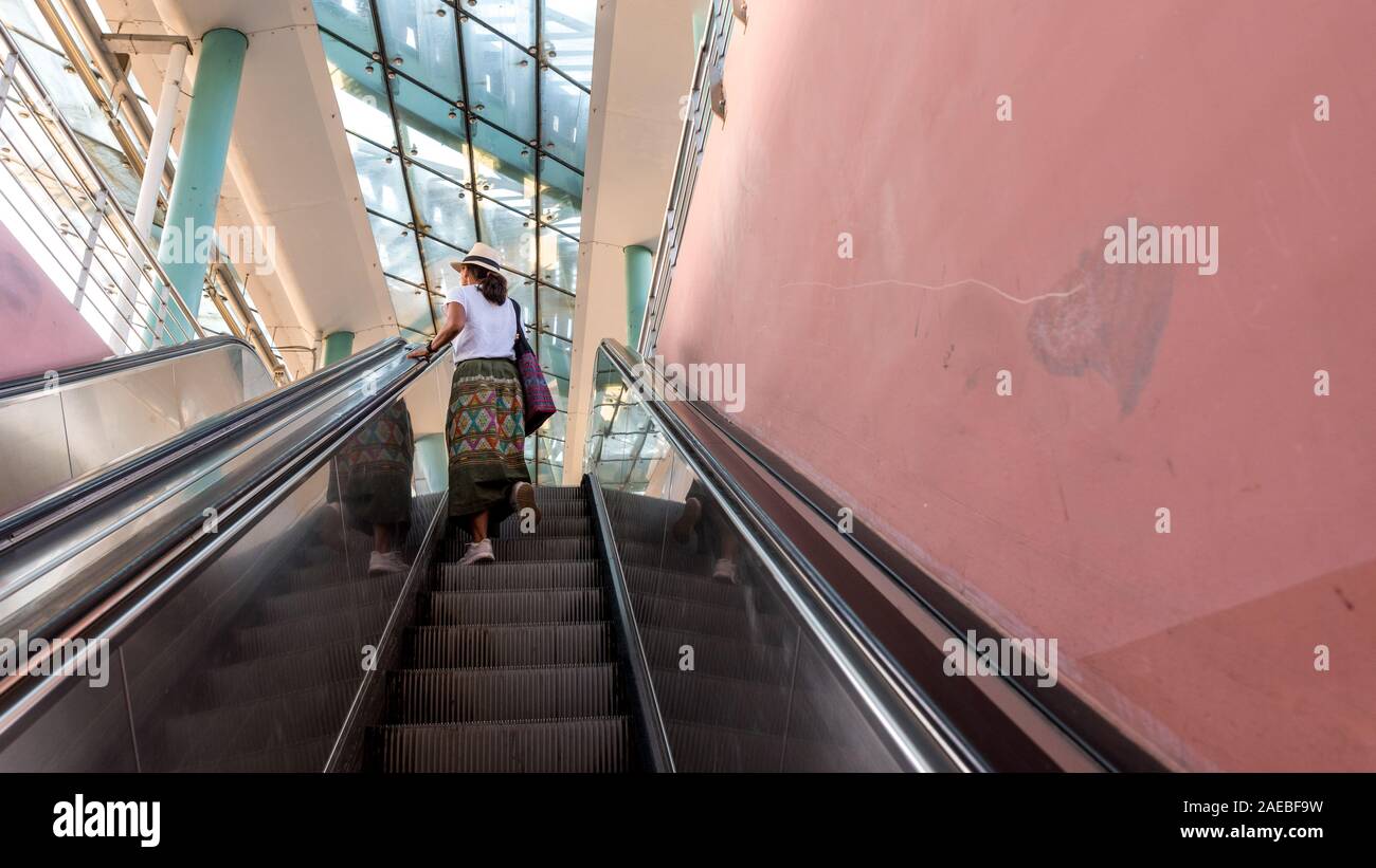 Asian woman riding up escalator in Metro station with pink walls and ...