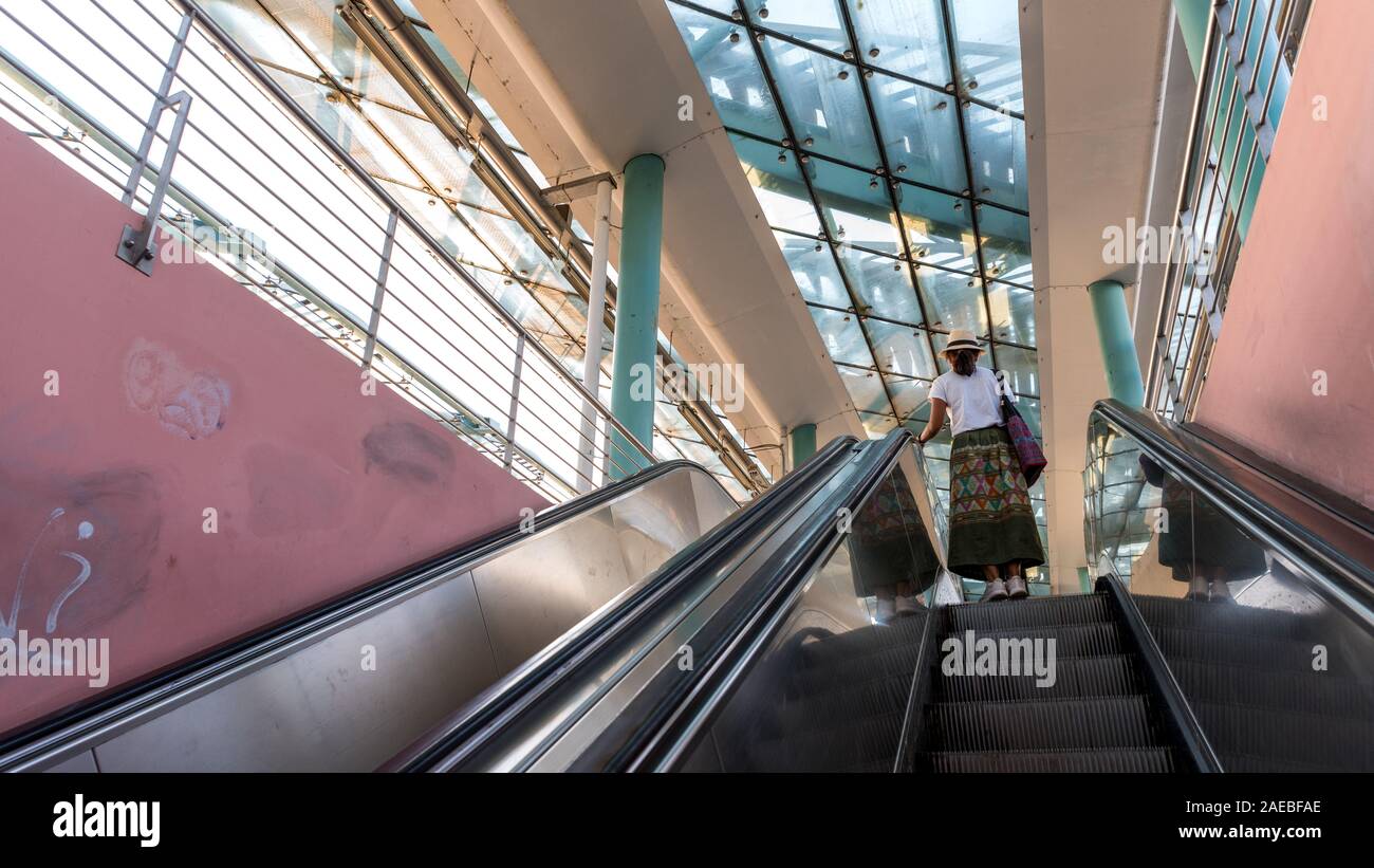 Asian woman riding up escalator in Metro station with pink walls and ...