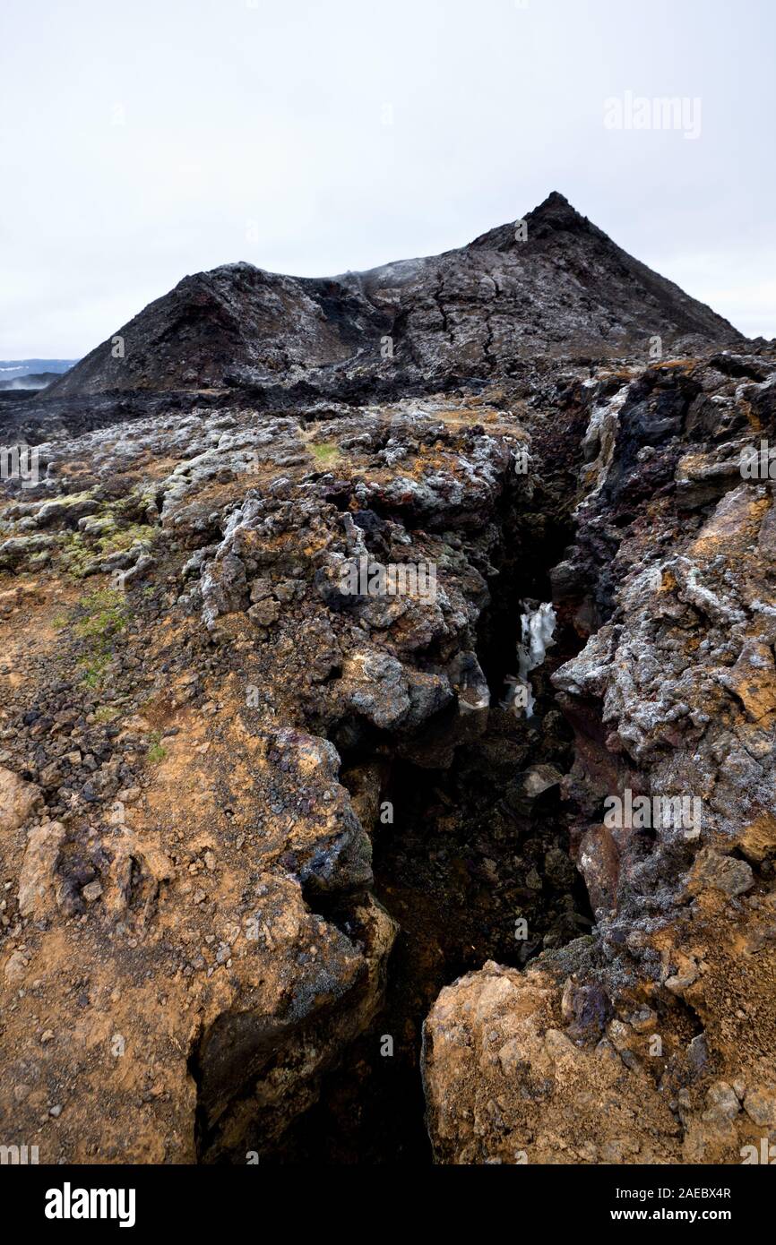 A deep chasm with a volcano crater in the background, seen in Iceland ...
