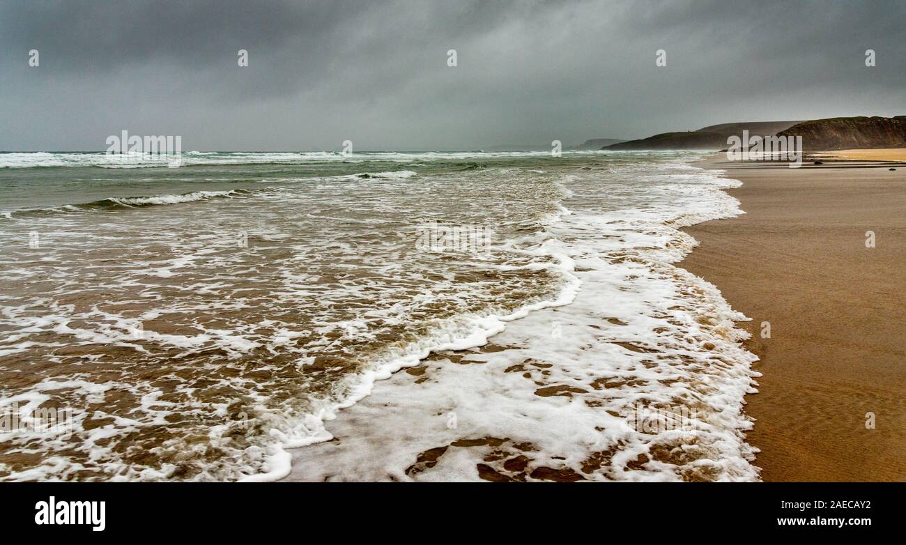 Sandy beach in winter in Brittany. The white foam of the waves of the ...